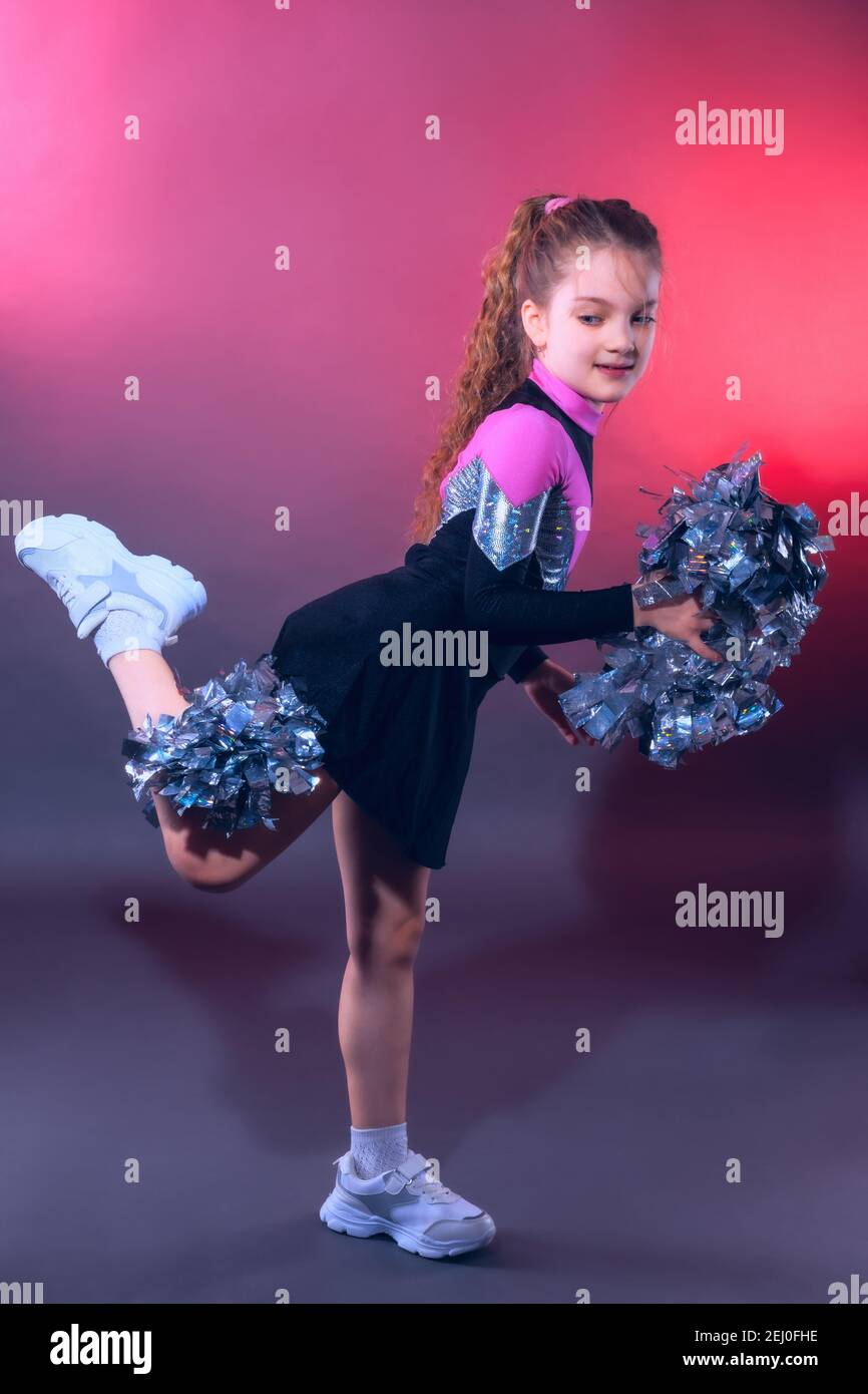 Little cheerleader practicing dance elements in studio with color light ...