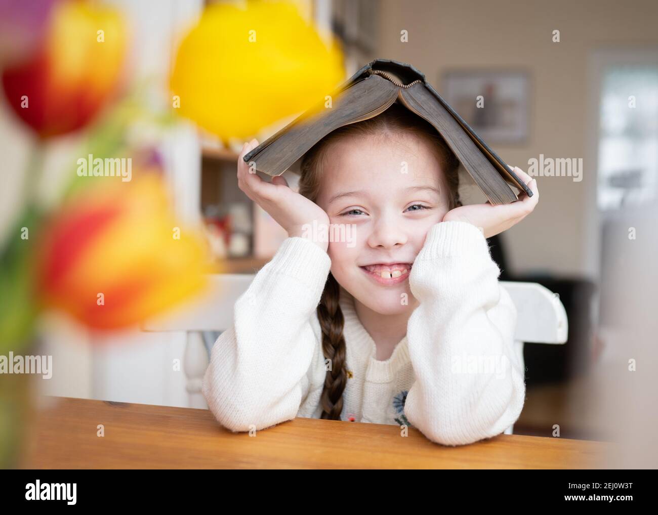 Beautiful happy young girl lockdown homeschooling with big book reading ...