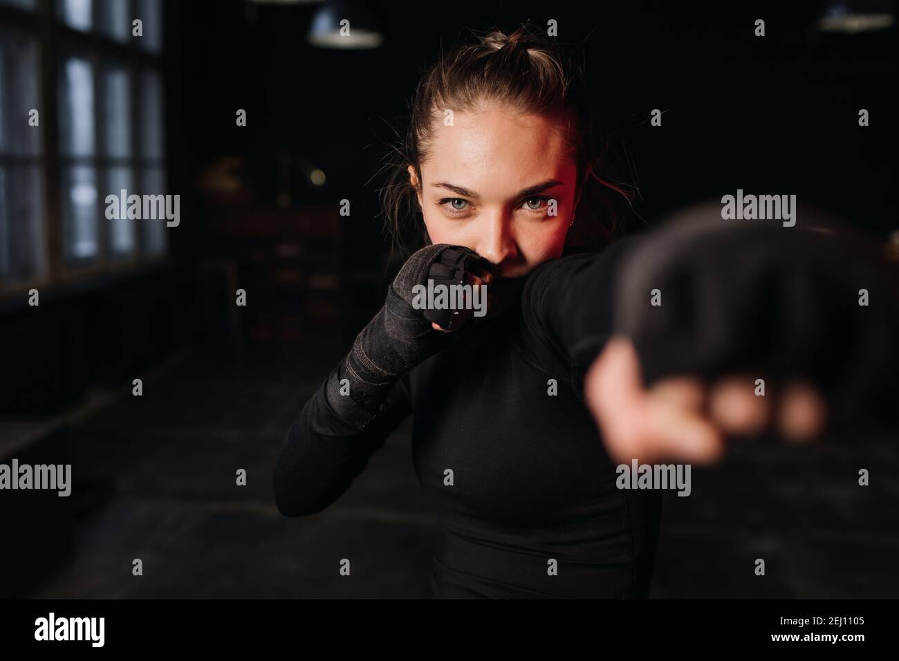 cool female fighter in boxing gloves trains in the gym. Mixed martial ...