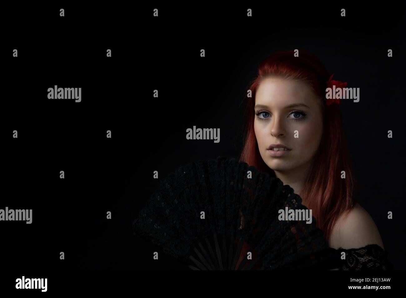 Low key portrait of beautiful young woman with fan looking at the ...