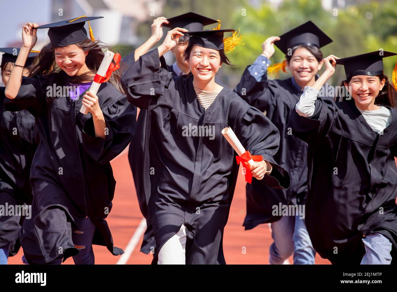 happy graduation students holding diploma and running on the stadium at ...
