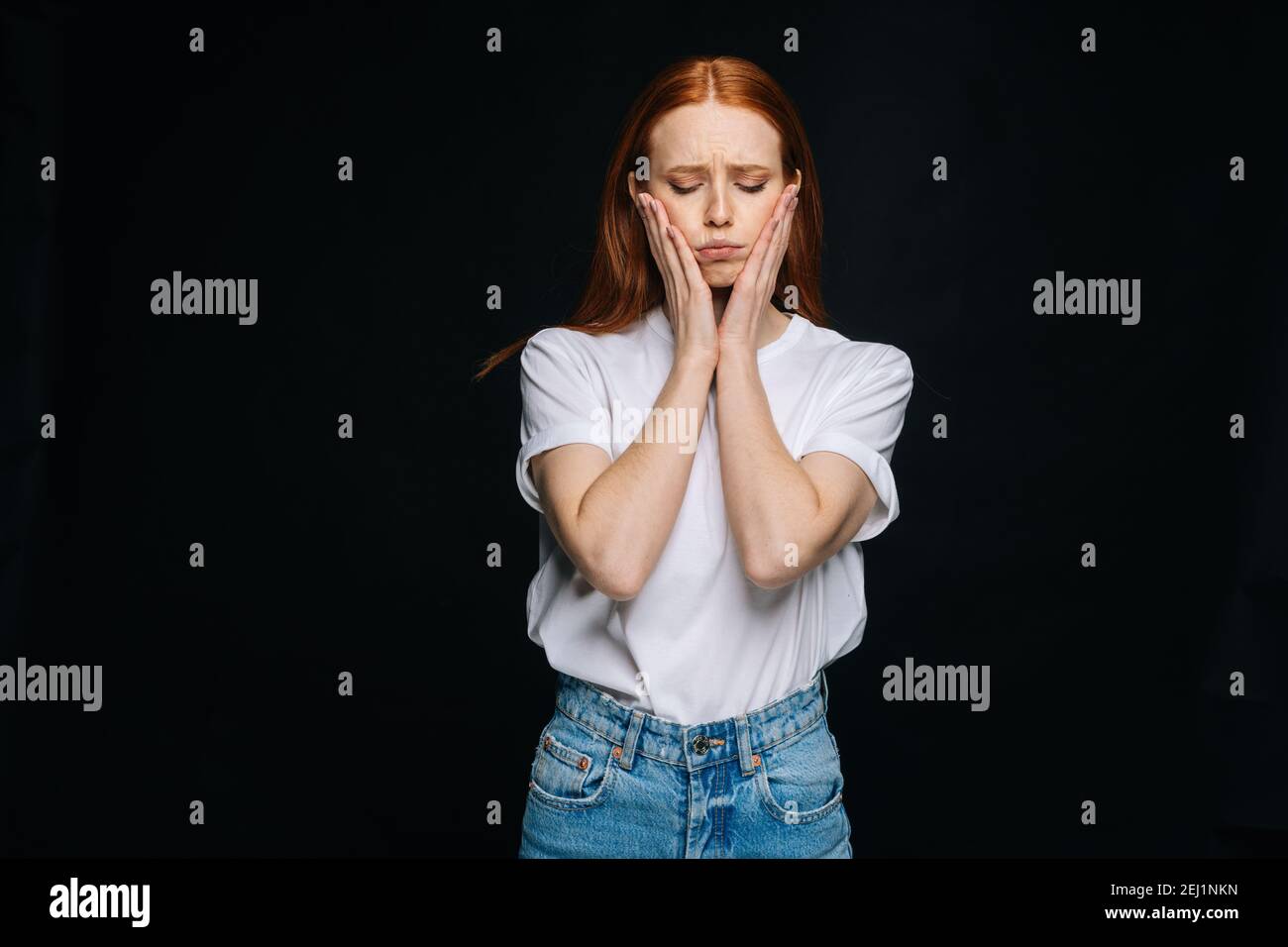 Sad unhappy young woman in T-shirt and denim pants standing on isolated ...