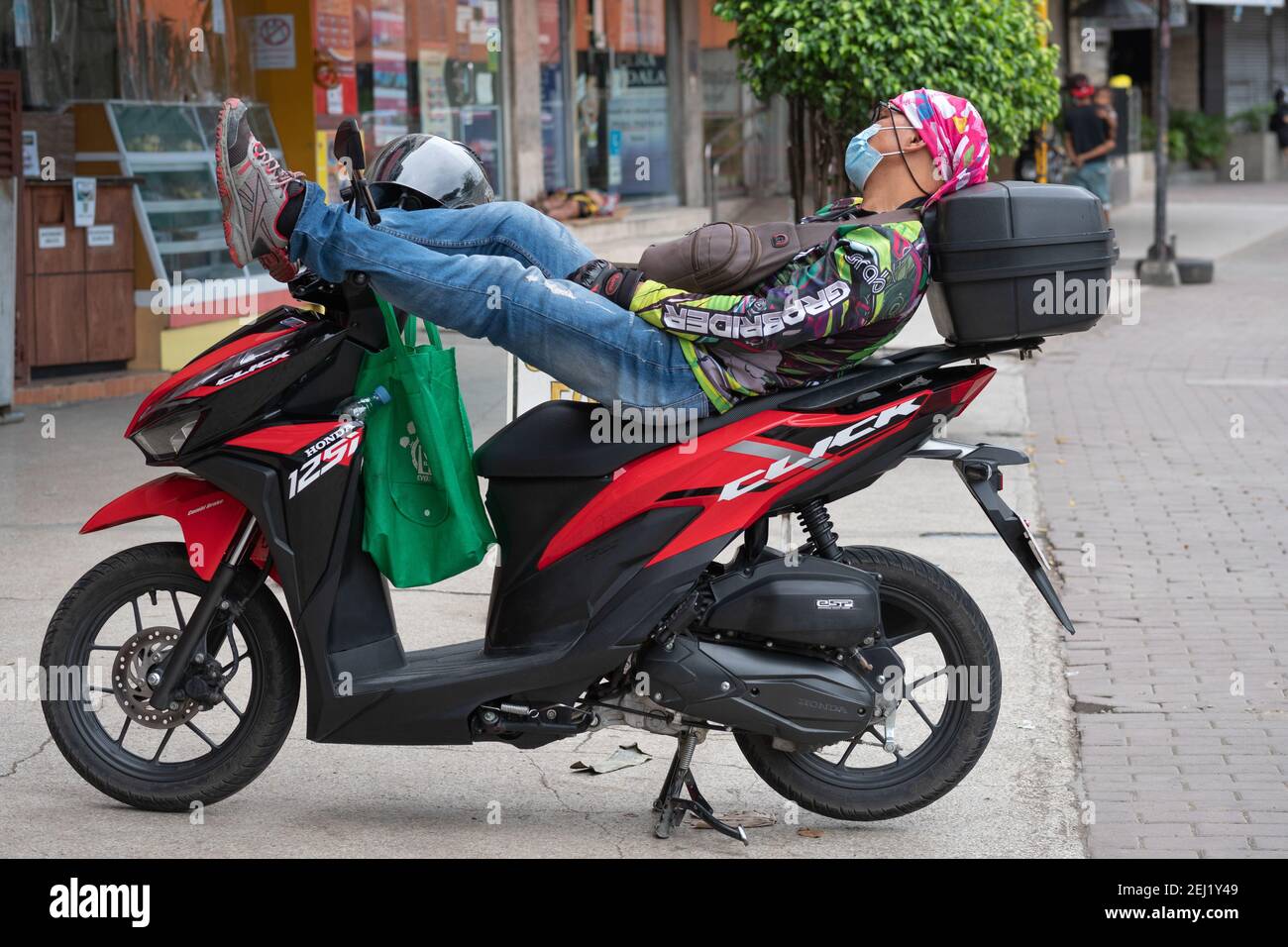A Filipino motorcycle rider sleeping on his motorcycle wearing a face ...