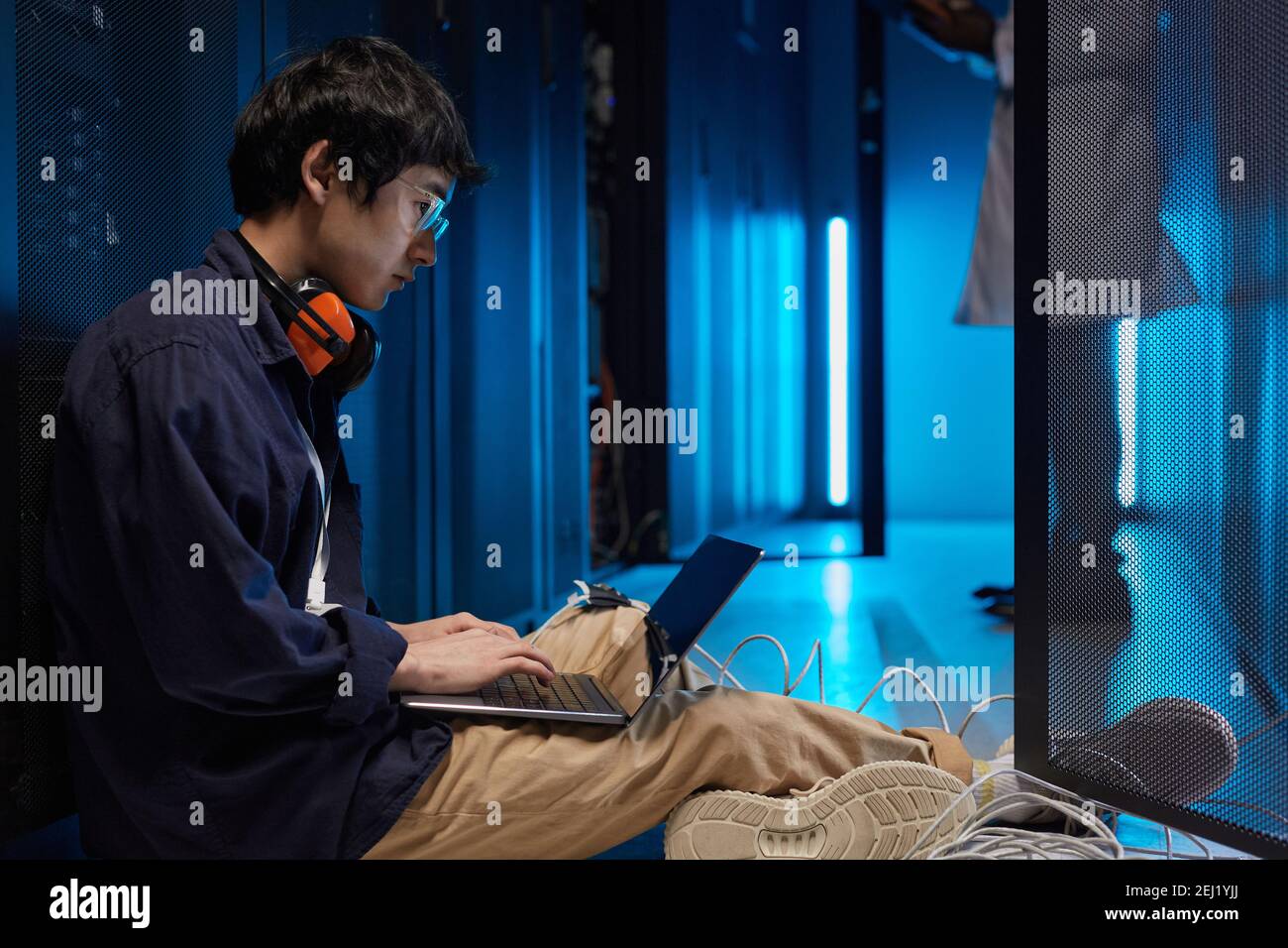 Side view portrait of young Asian man sitting on floor in server room ...