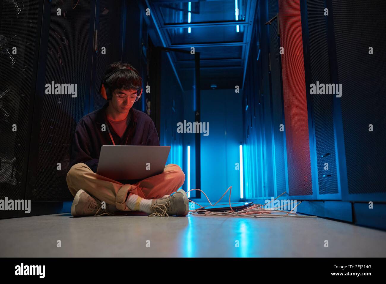 Full length portrait of young Asian man using laptop while sitting on ...