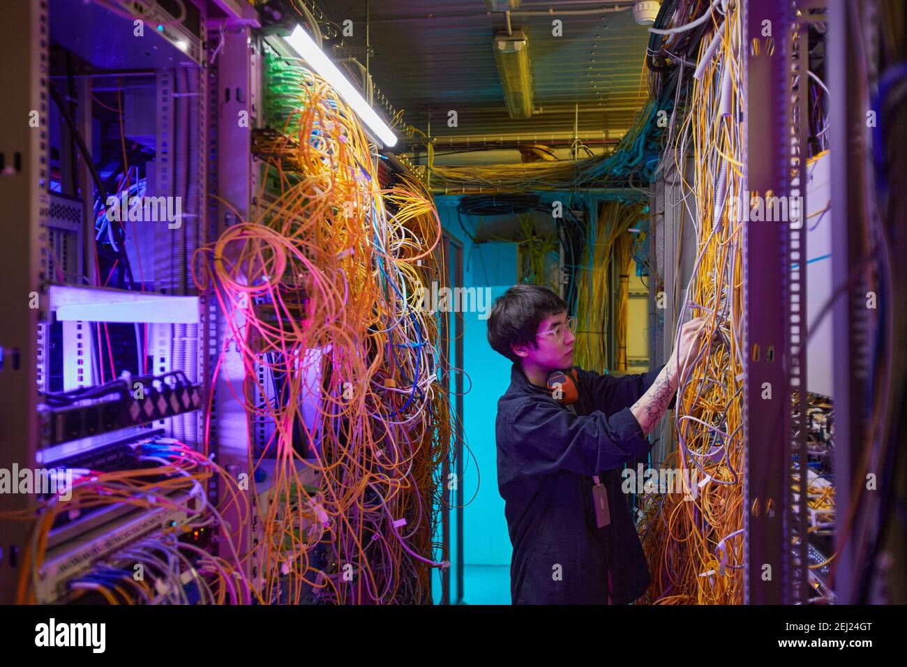 Wide angle side view at young network technician connecting wires and ...