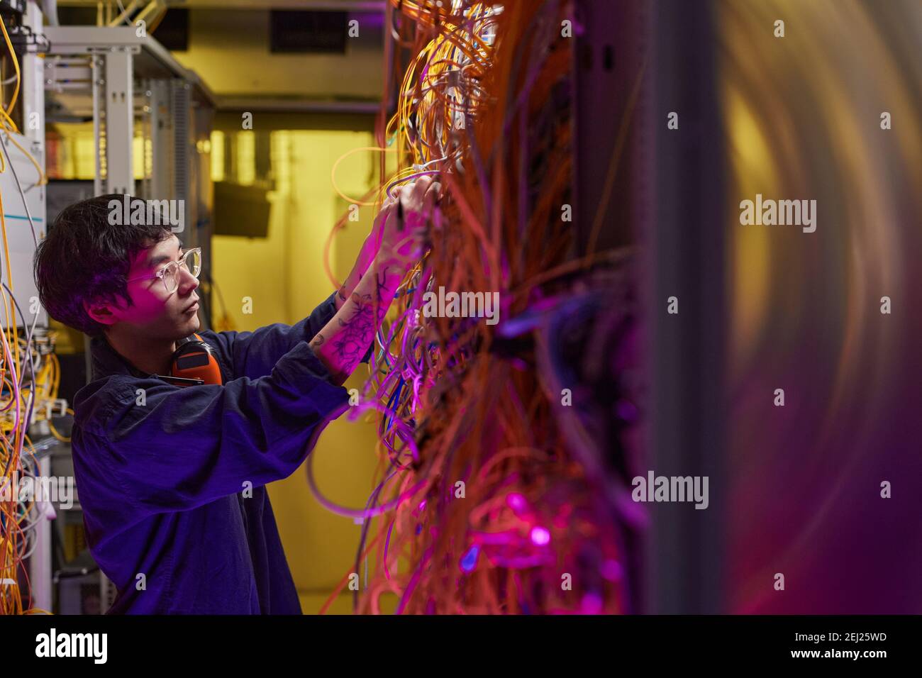 Wide angle portrait of young network technician connecting wires and ...