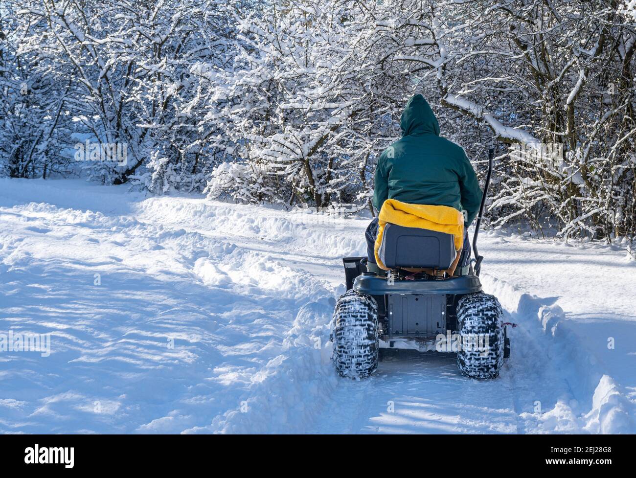A rear view of a man riding snow blower clearing a snow-covered field ...