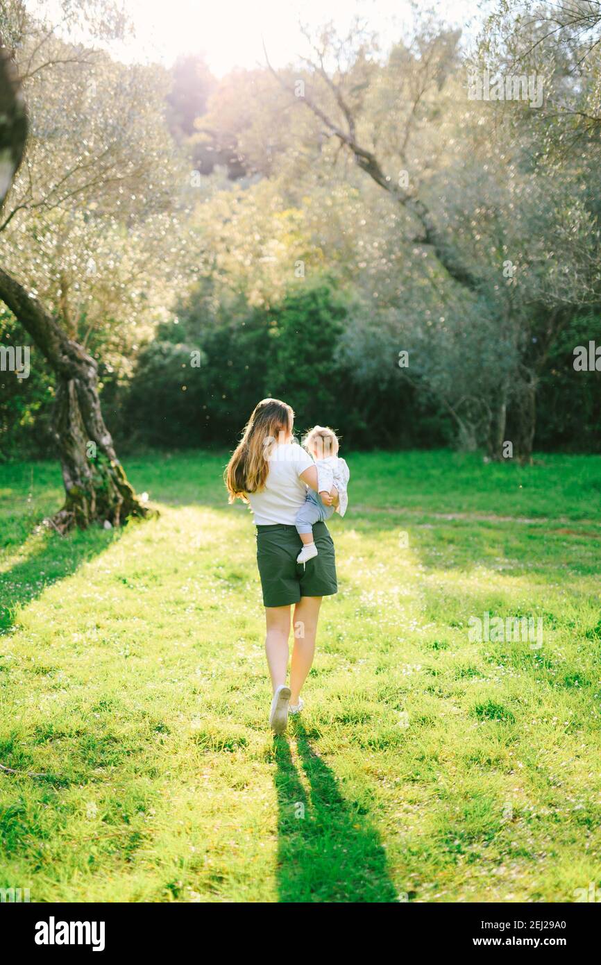 Woman walking under an olive tree with her daughter in her arms Stock ...