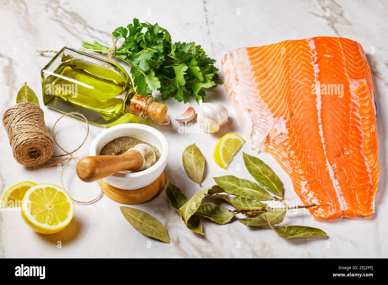 raw salmon fillet on a marble table with bay leaves, parsley, olive oil ...