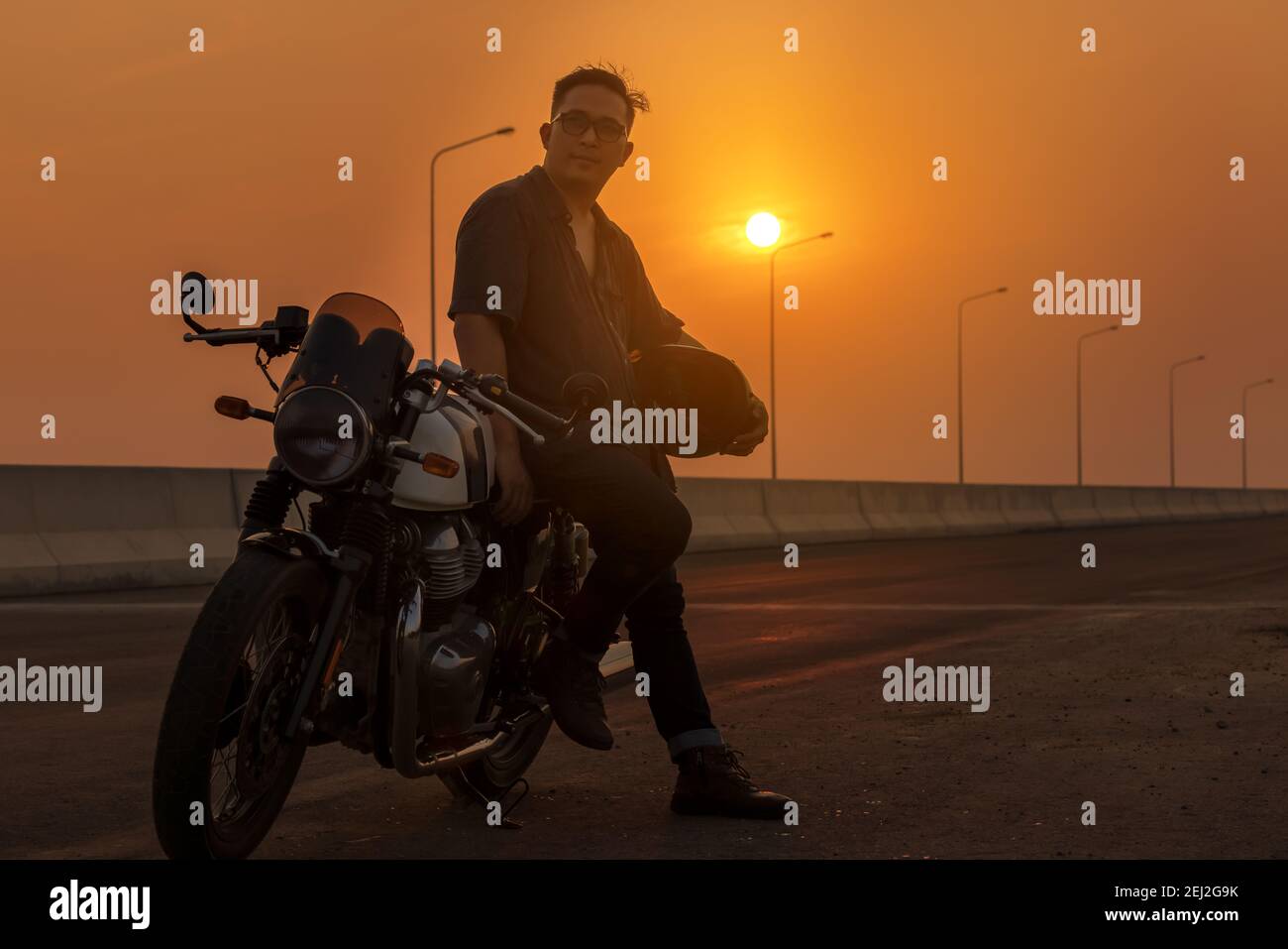 Motorcycle driver in a helmet and leather jacket stands on the road ...