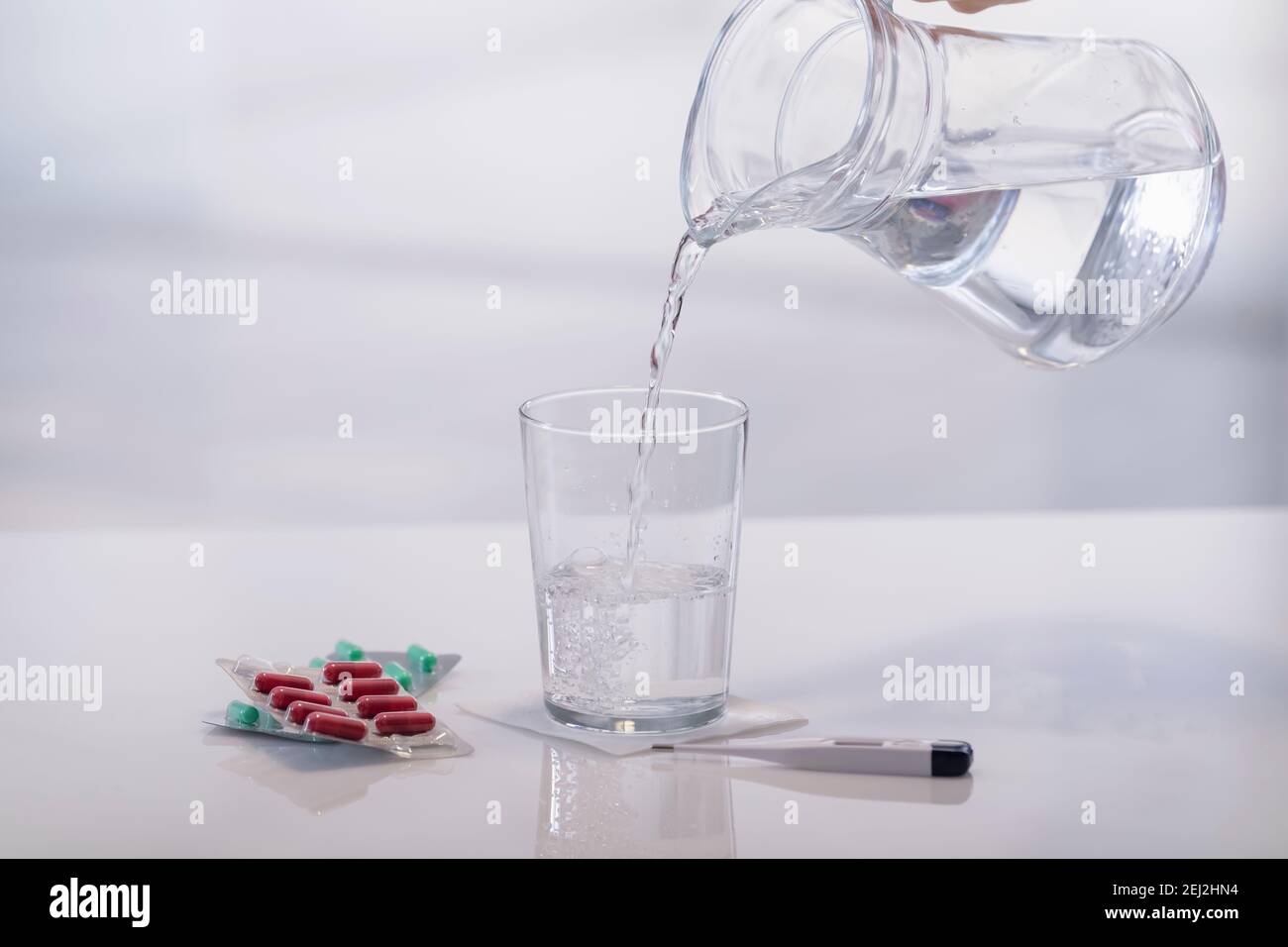 Close up of a hand pouring water into a glass surrounded by medication ...