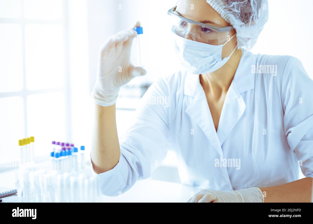 Professional female scientist in protective eyeglasses researching tube ...