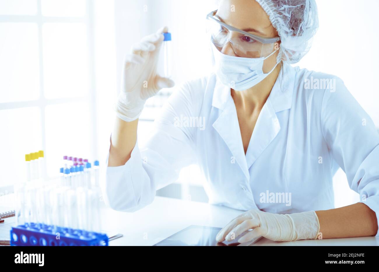 Professional female scientist in protective eyeglasses researching tube ...