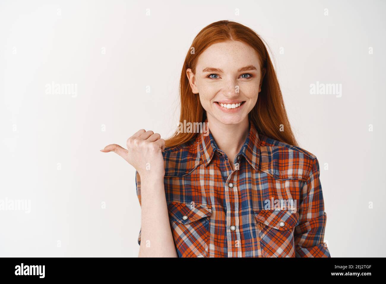 Shopping. Young redhead lady pointing thumb left and smiling, showing ...