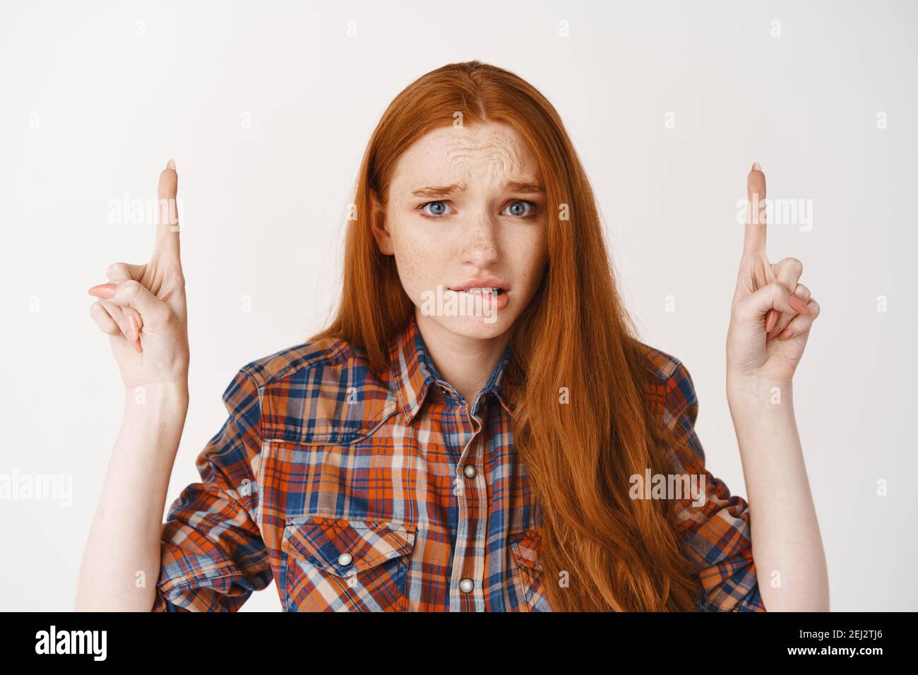 Young redhead woman biting lip with complicated look, pointing fingers ...
