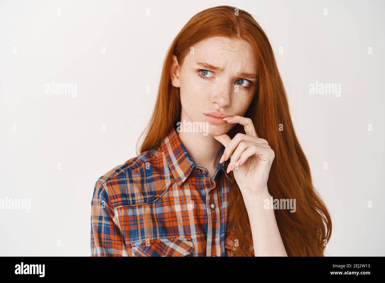 Puzzled redhead girl looking complicated, touching lip and frowning ...