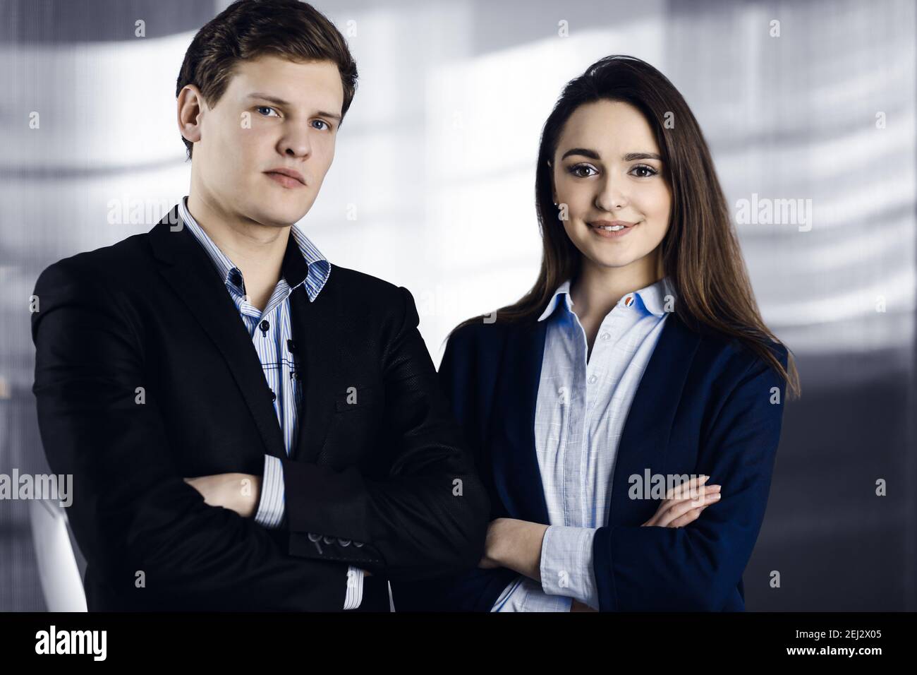 Friendly young colleagues are standing as a team with crossed arms in a modern office. Portrait ...