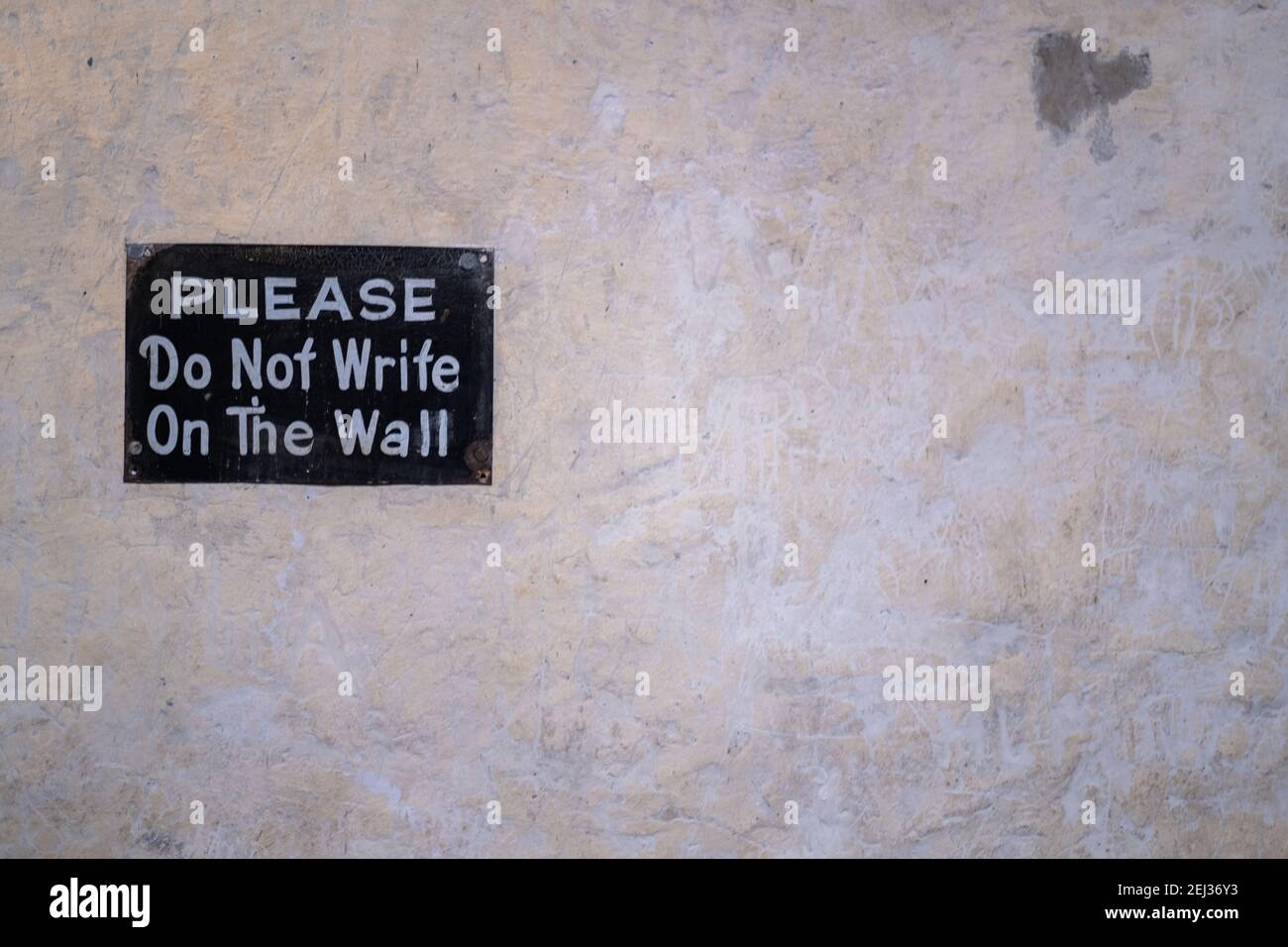 A black warning signboard saying please do not write on the wall in ...