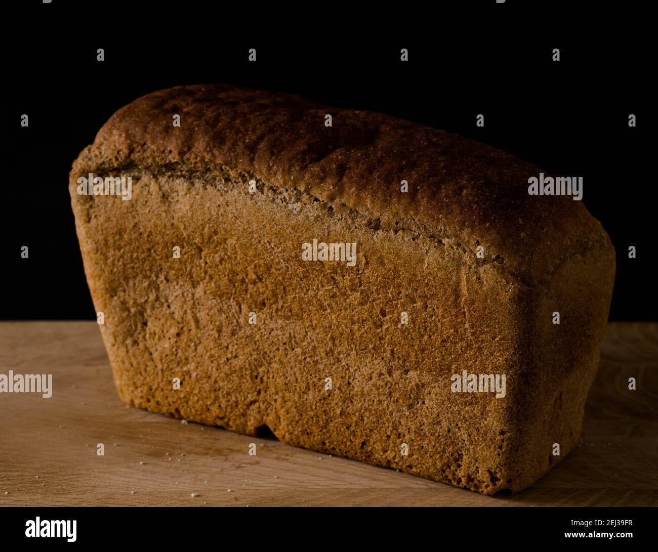 Loaf of black rye bread, in the shape of a brick, on a wooden board on ...