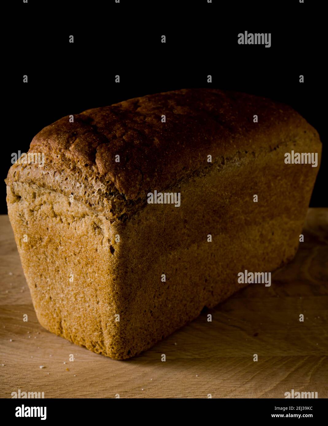 Loaf of black rye bread, in the shape of a brick, on a wooden board on ...