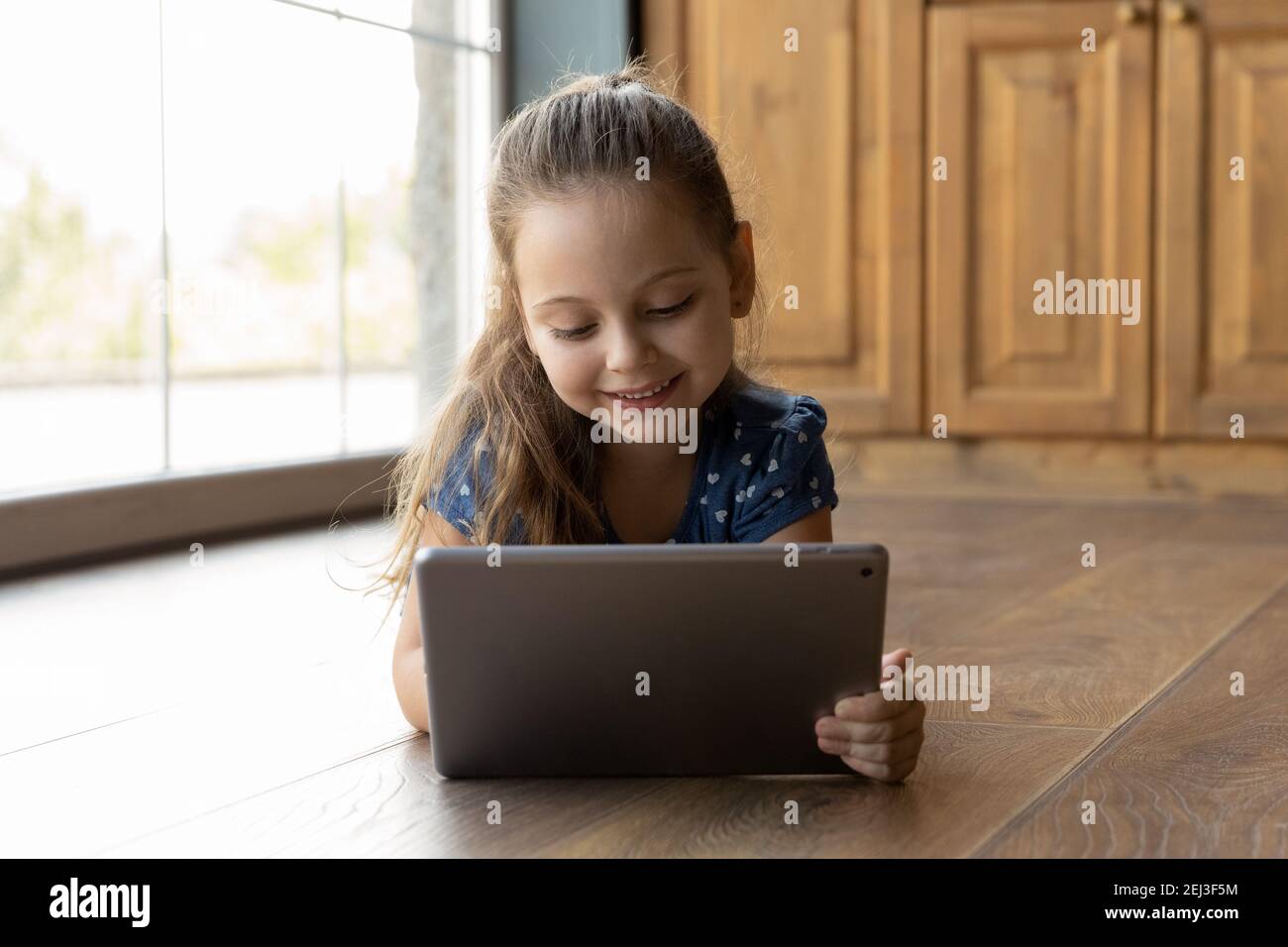 Close up smiling little girl using tablet, lying on floor Stock Photo ...