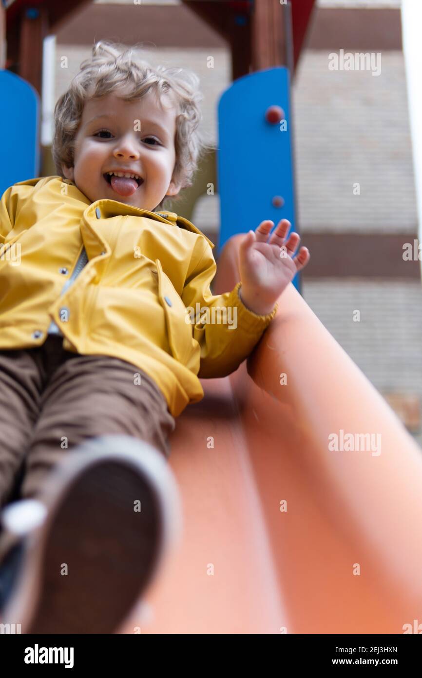 happy and smiling two-and-a-half-year-old boy jumping down a slide in a ...