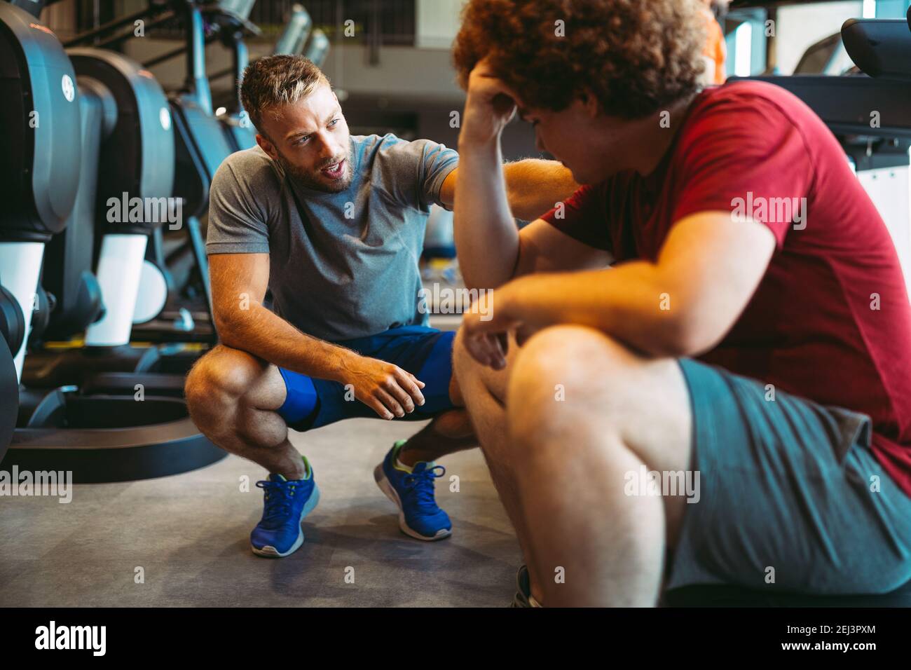 Overweight young man exercising gym with personal trainer Stock Photo ...
