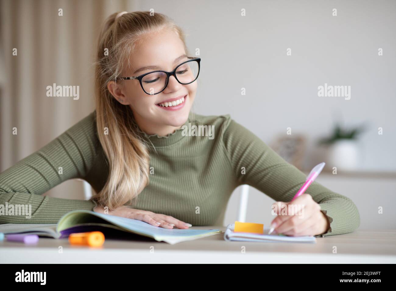 Cute blonde school girl doing homework and smiling Stock Photo - Alamy
