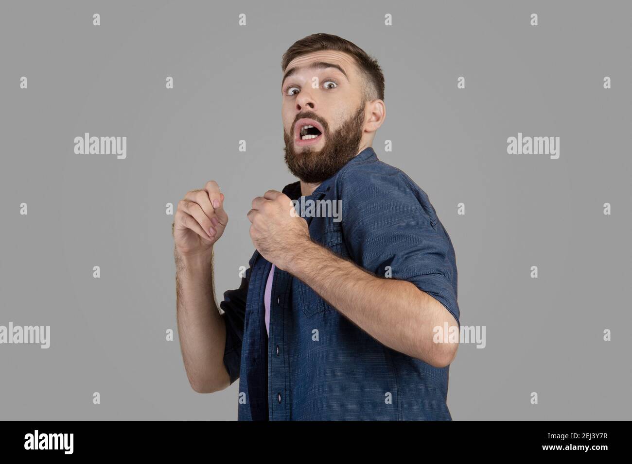Young hipster guy being scared or terrified over grey studio background ...