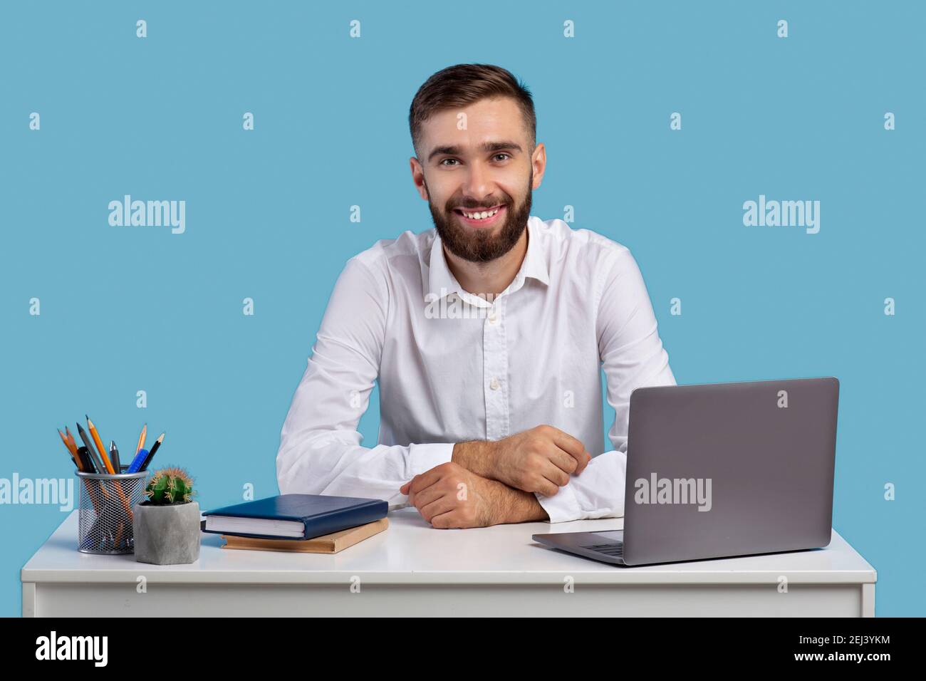 Successful young office worker sitting at desk with laptop computer and ...