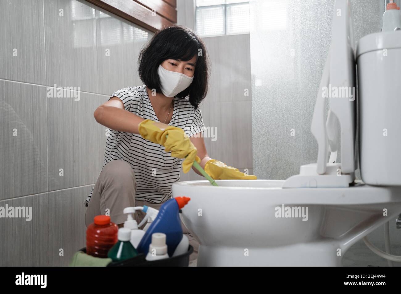 housewife wearing a mask wearing gloves brushing the dirty toilet in ...