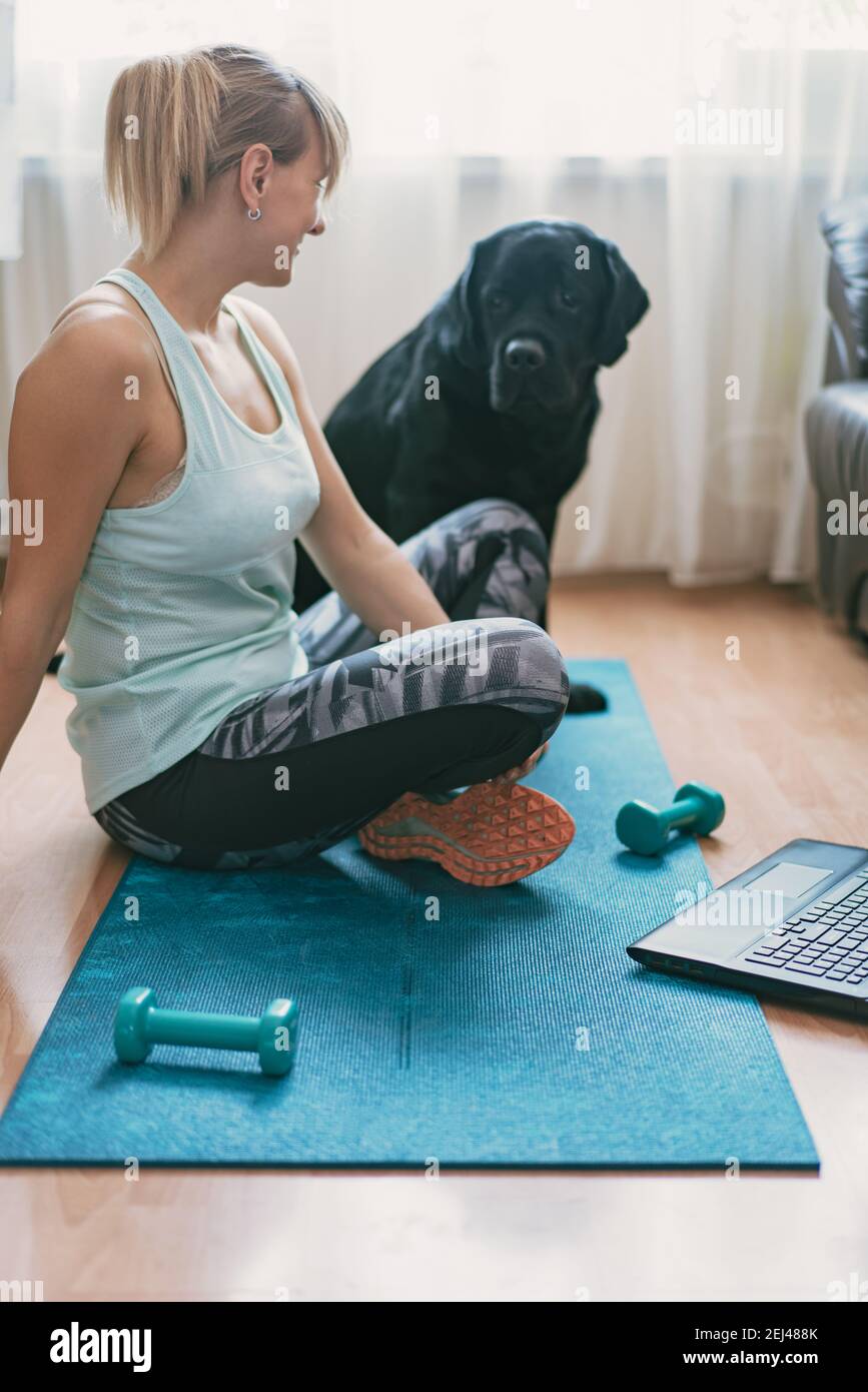 Shot of a woman doing exercise at home while her dog sitting next to ...