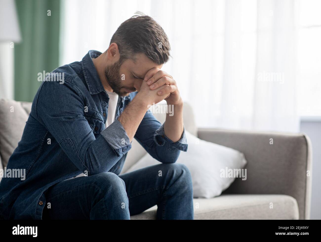 Depressed man sitting on couch in living room Stock Photo - Alamy