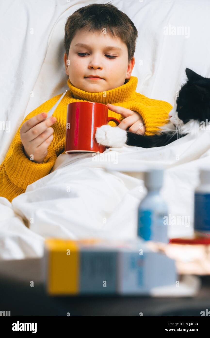 Sick child boy with digital thermometer in mouth lying in bed with ...