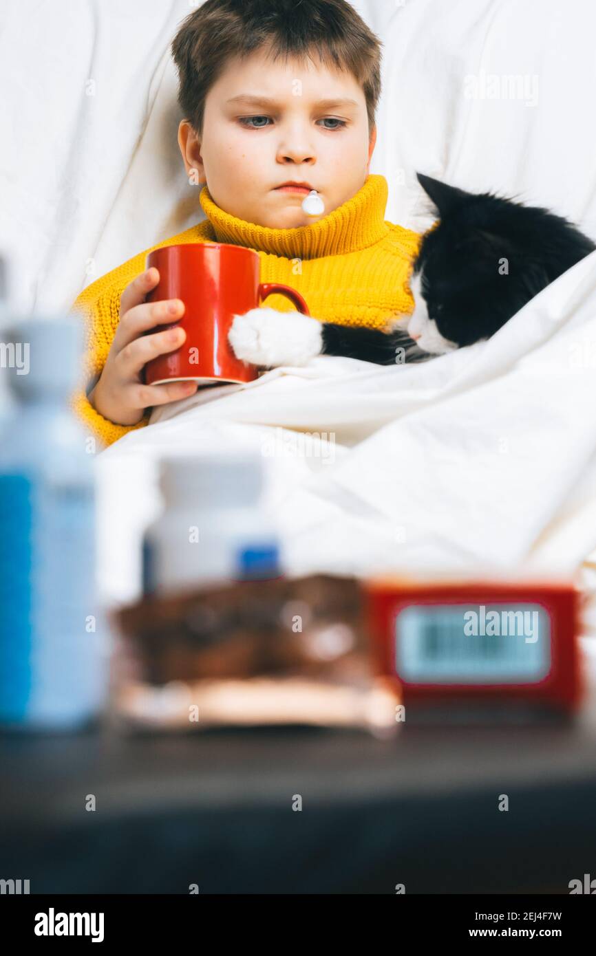 Sick child boy with digital thermometer in mouth lying in bed with ...