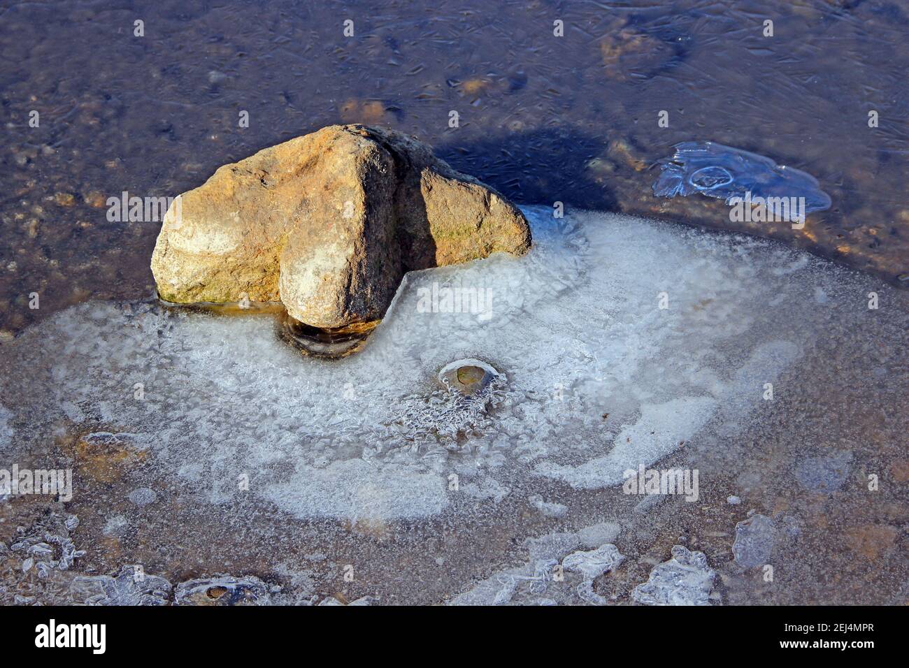 Top view of a rock in the water. The cold water is partially frozen ...