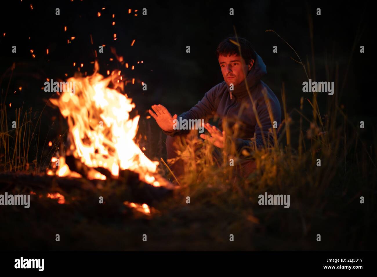 Young man making fire while camping outdoors, in an alpine wilderness ...