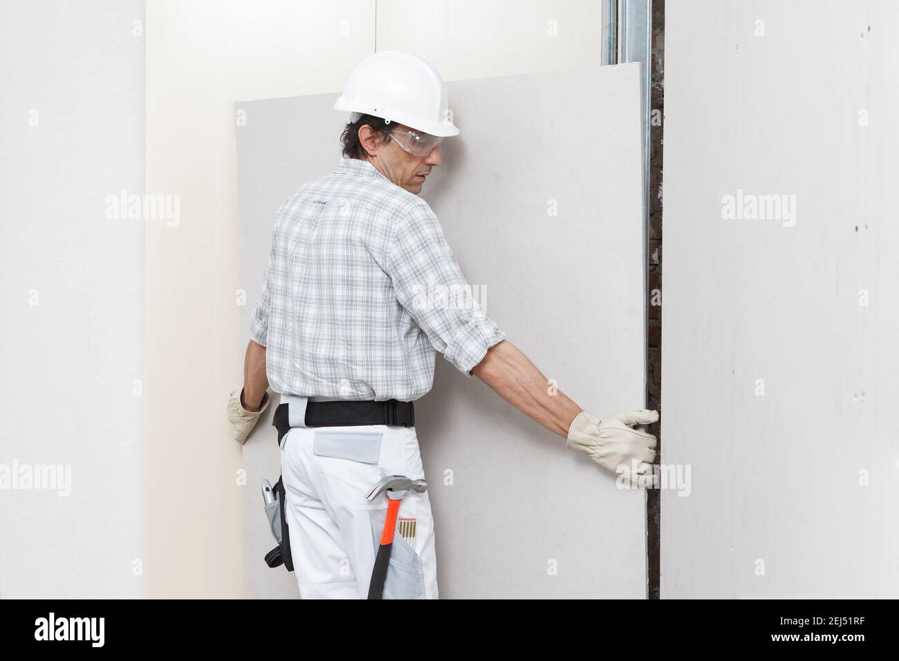 man drywall worker installing plasterboard sheet to wall. Wearing ...