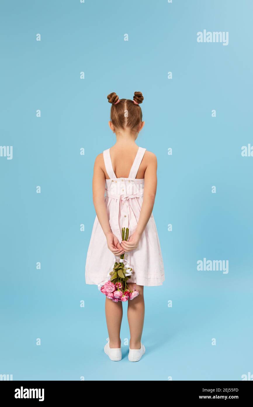 little girl holding bouquet of roses behind her back on blue studio ...