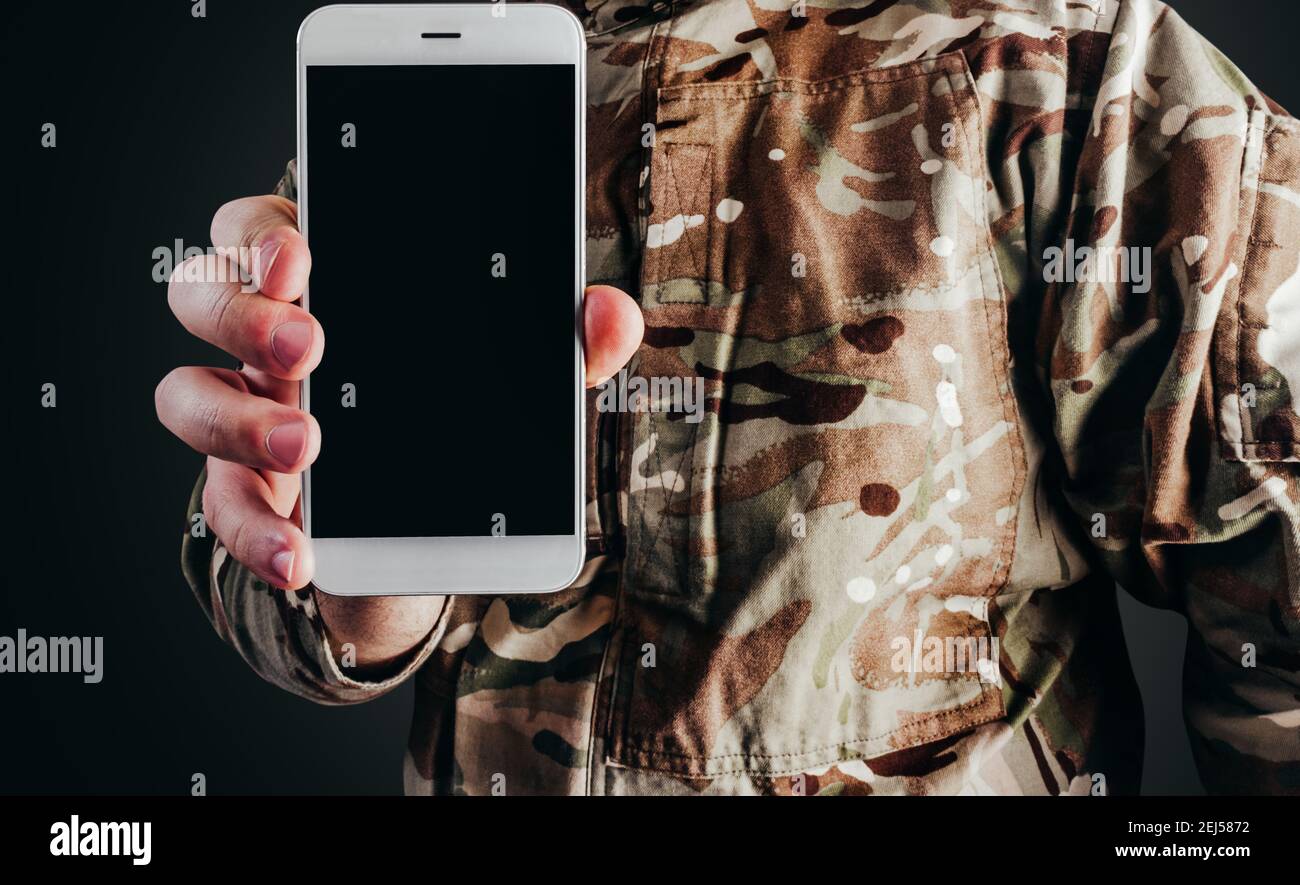 Photo of soldier in camouflaged uniform holding smartphone on black ...