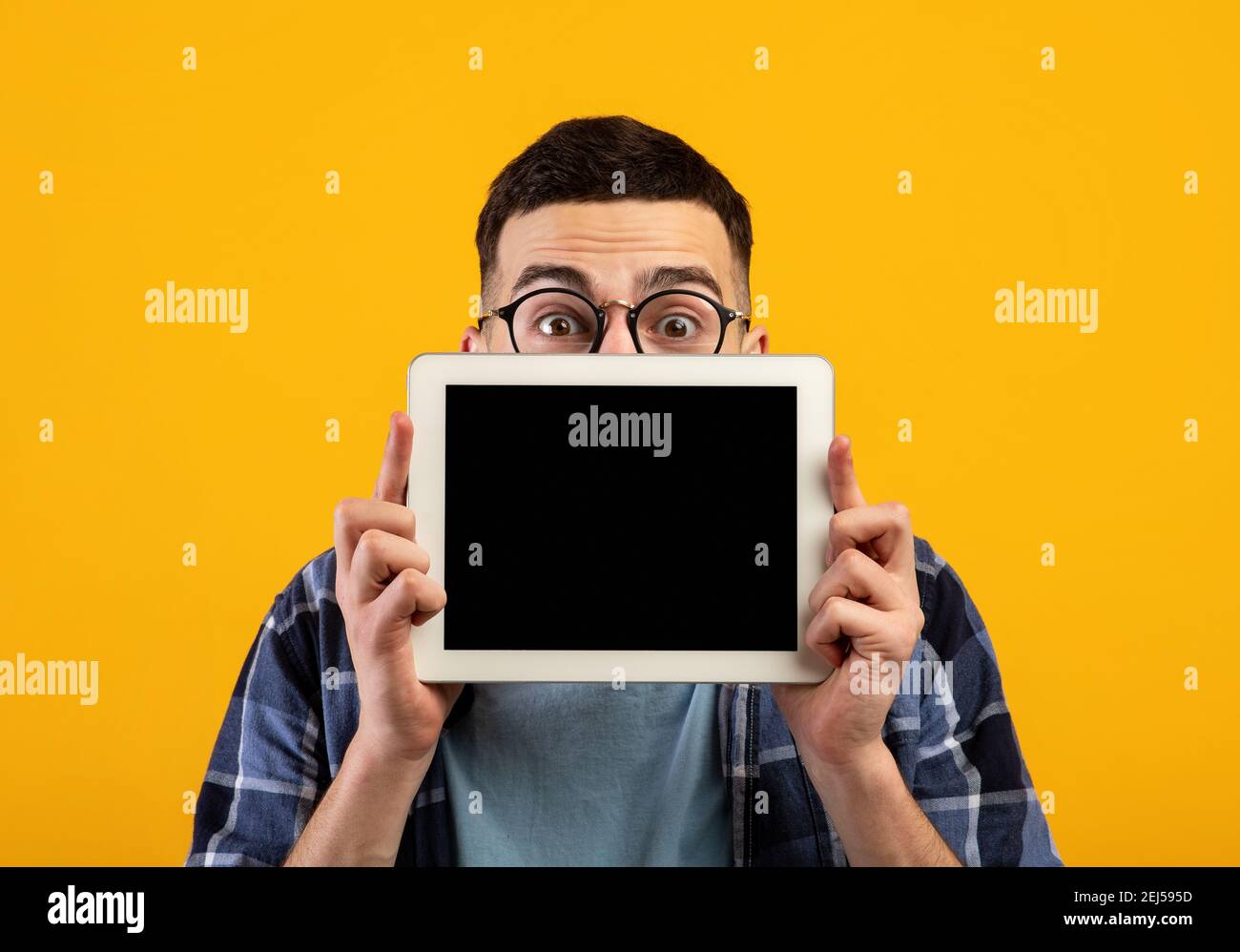 Shocked young guy hiding behind tablet computer with blank screen on ...