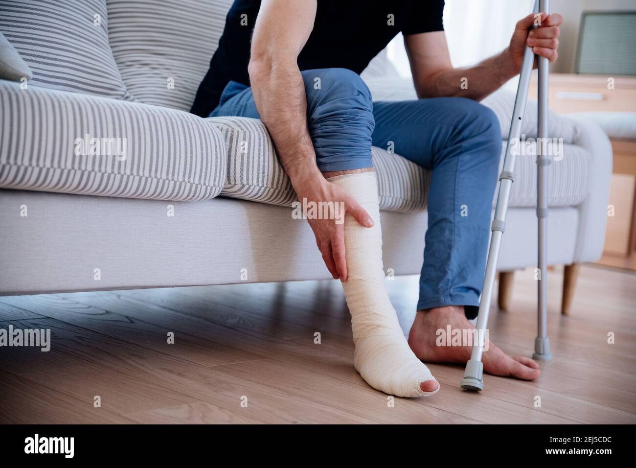 A young man with a broken leg sits on a sofa with a white plaster on ...