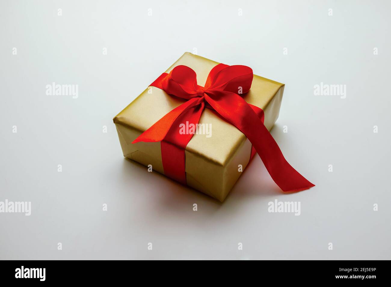 A holiday gift. Box in a gold gift wrapping with a red bow, on a white ...