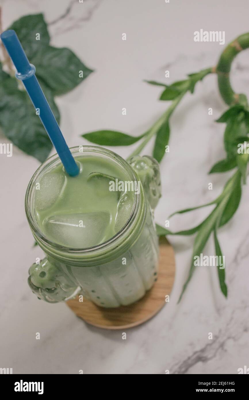 Vertical image of crystal glass full of Iced Matcha Tea on white marble ...