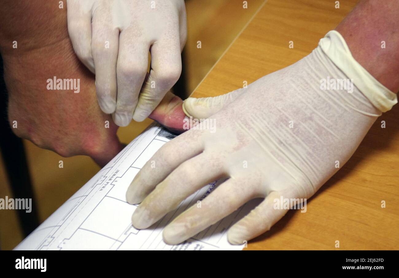A police officer wearing rubber gloves takes a fingerprint of a suspect ...