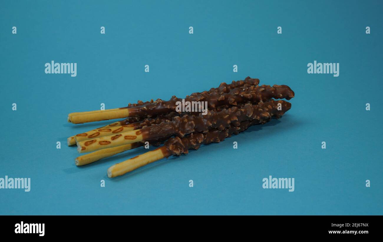 Crispy sticks with hazelnut sprinkles in chocolate on a blue background ...