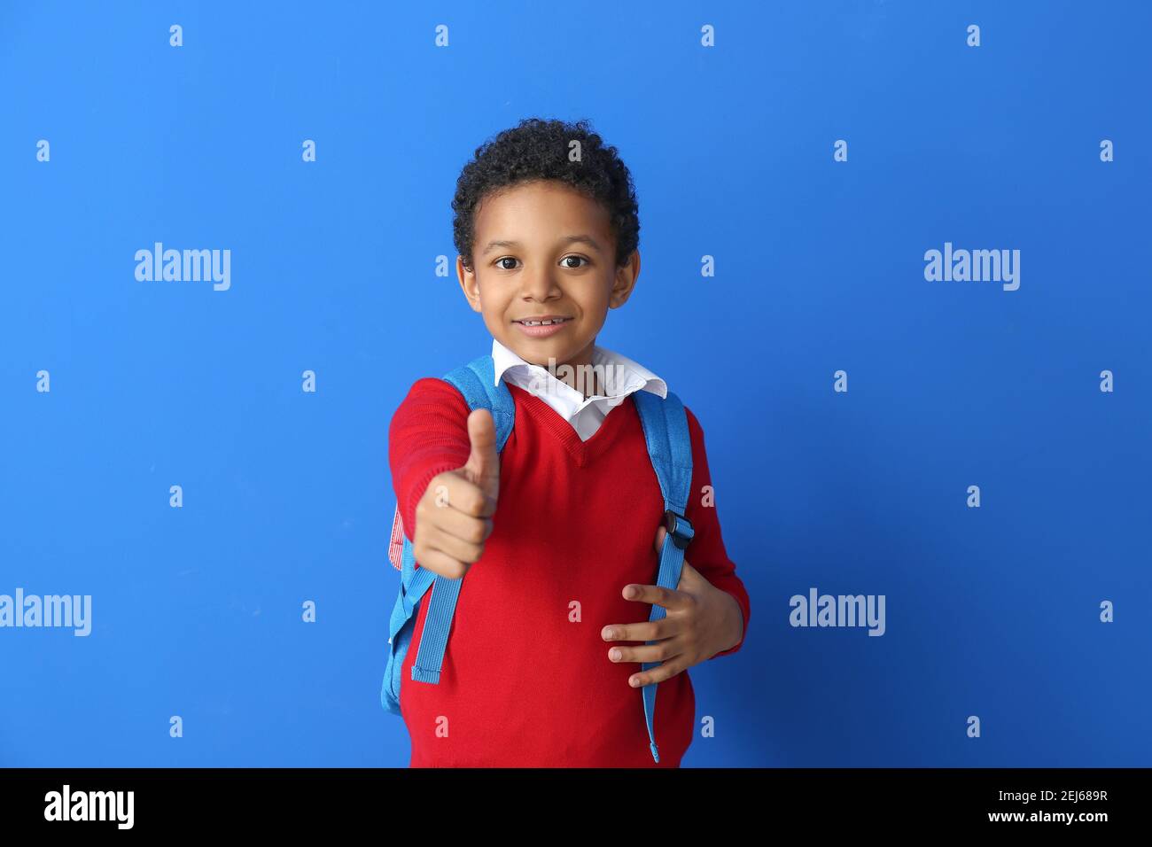 Little African-American schoolboy showing thumb-up gesture on color ...