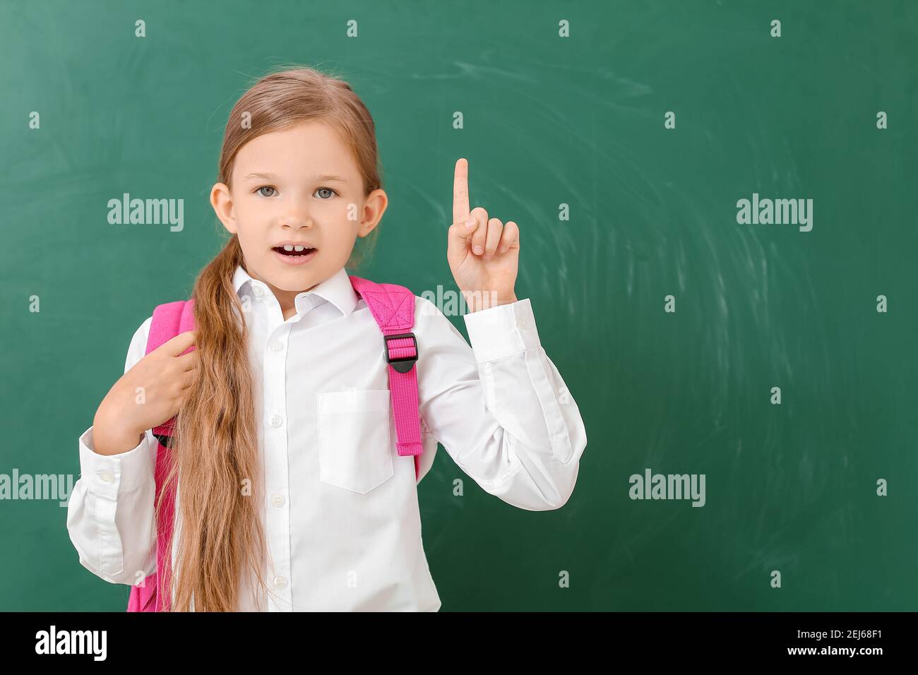 Little schoolgirl with raised index finger near chalkboard in classroom ...
