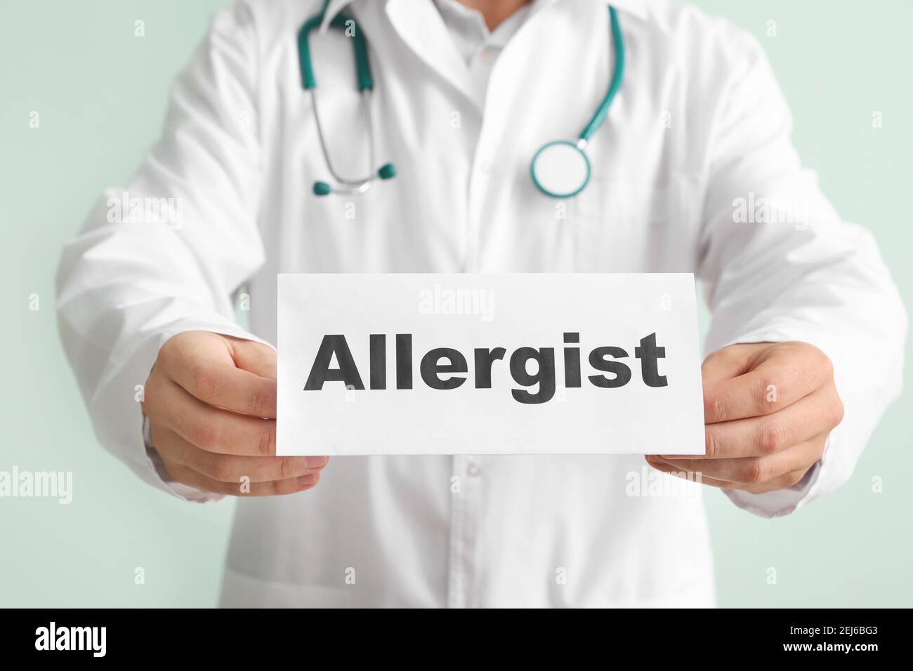 Doctor holding paper with word ALLERGIST on color background, closeup ...